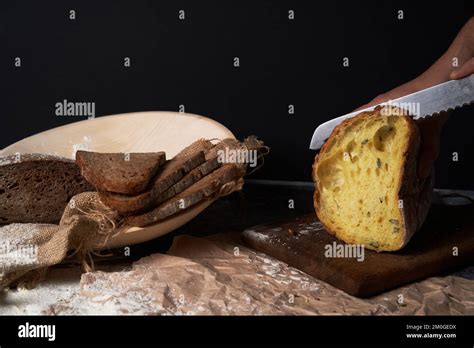 Mens Hands Cut A Loaf Of Bread On A Cutting Board On A Dark Black