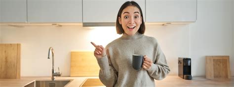 Retrato De Uma Menina Asiática Sorridente Em Pé Na Cozinha Tomando