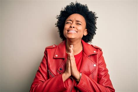 젊은 아름 다운 아프리카 계 미국인 Afro 여자 곱슬 머리 캐주얼 빨간 재킷을 입고 구걸 하 고 매우 감정적이 고 걱정 얼굴에 희망 표정과 함께 손으로 기도 구걸