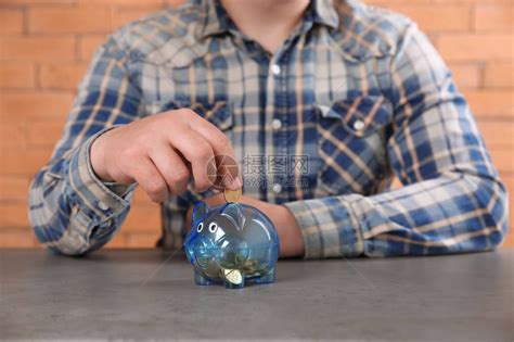 男人把硬币放进桌子上的存钱罐里高清图片下载 正版图片505263619 摄图网