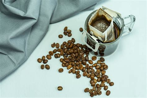 분쇄 커피 커피 방울 용 가방 및 테이블 위의 투명한 머그잔 커피 원두가있는 회색 배경에 커피를 떨어 뜨립니다 커피는 쿡을 사용하여 드립 추출하여 준비합니다 0명에 대한