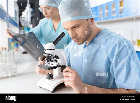 Side View Of Surgeon Looking Through Microscope And Doctor Analyzing X