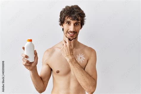 Young Hispanic Man Standing Shirtless Holding Sunscreen Lotion Looking