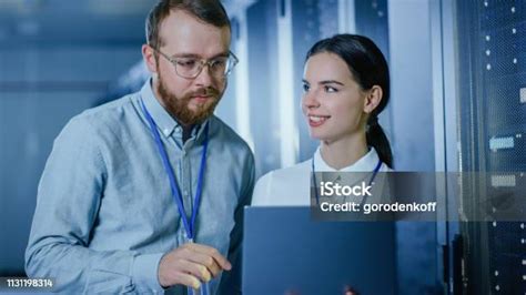 수염 있는 It 기술자와 노트북 컴퓨터와 아름 다운 젊은 엔지니어 동료는 서버 랙 옆에 작업 하는 동안 데이터 센터에서 얘기 하 고 있습니다 진단을 실행 하거나 유지 보수