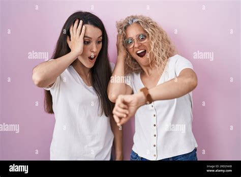 Mother And Daughter Standing Together Over Pink Background Looking At