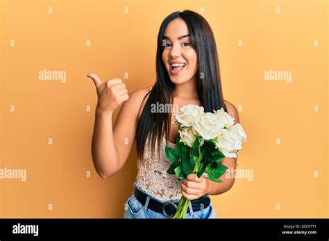 Young Beautiful Hispanic Girl Holding Bouquet Of White Flowers Pointing