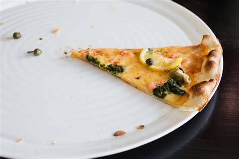 흰색 도자기 접시에 해산물 허브 치즈 토마토 레몬 조각과 황금 향기로운 피자의 조각 블랙 테이블에 이탈리아 국가 접시 재료의 많은 작품의 케이크 높은 칼로리 식품 자연