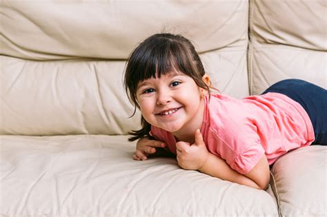 A Girl Lying And Smiling On A Cream Sofa In A Pink Tshirt And Blue