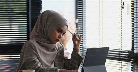 히잡을 쓴 무슬림 사업가의 초상화는 사무실에서 태블릿으로 생각하고 작업하고 있다 사진 Unsplash의 태국 이미지