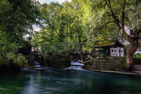 Serene Riverside Scene With Waterfall And Bridges In A Lush Village