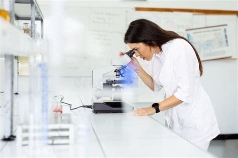Side View Of Young Female Scientist Looking Through Microscope Stock