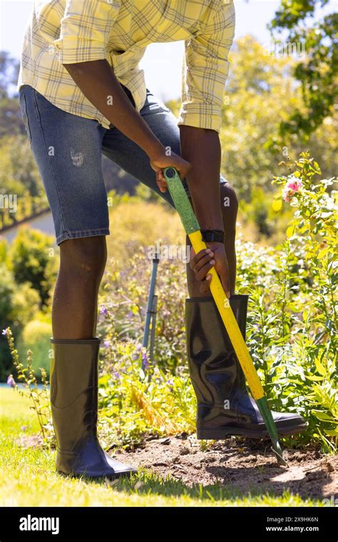 An African American Young Male Digging Outside Wearing Boots And