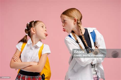 Two Schoolgirls Sticking Out Tongues At Each Other On Pink Background