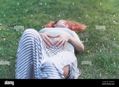 Pregnant White Girl Lies On Green Grass In A Light Striped Dress On A