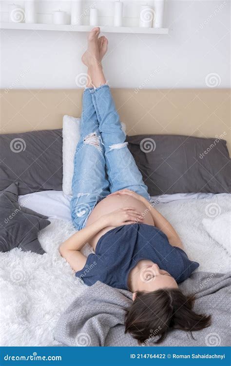Pregnant Woman Dressed Jeans And T Shirt Lying On Bed Relaxing With