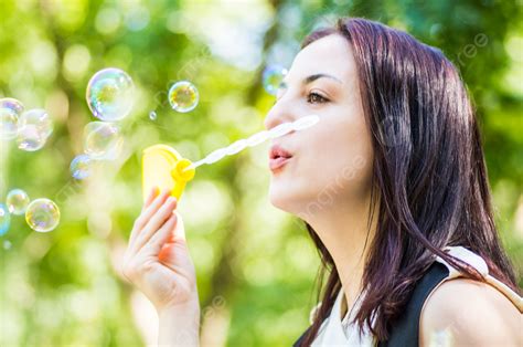 A Caucasian Woman In Her Youth Blowing Soap Bubbles Amidst The Greenery