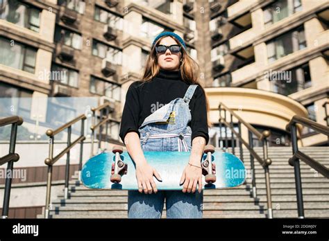 Stylishly Dressed Woman In Blue Denim Jumpsuit Posing With Skateboard