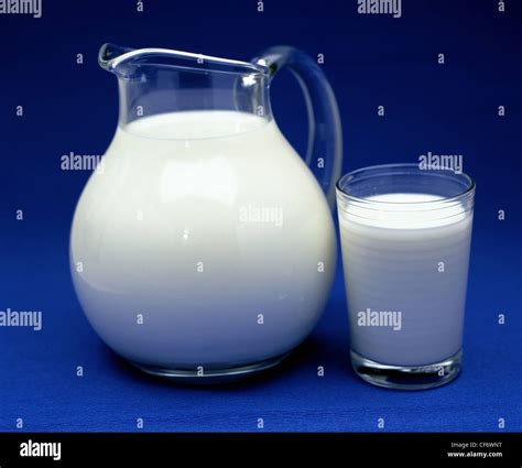 Large Glass Jug Of Milk And Glass Of Milk Against Blue Background Stock