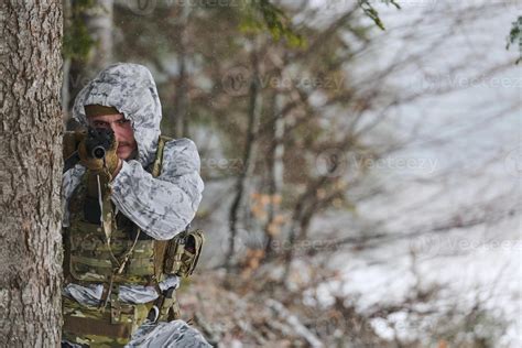 Soldier In Winter Camouflage Taking Aim Behind Tree During Cold Weather