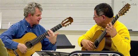 Two Men Are Playing Guitars In Front Of Music Instruments On The Table And One Man Is Wearing A