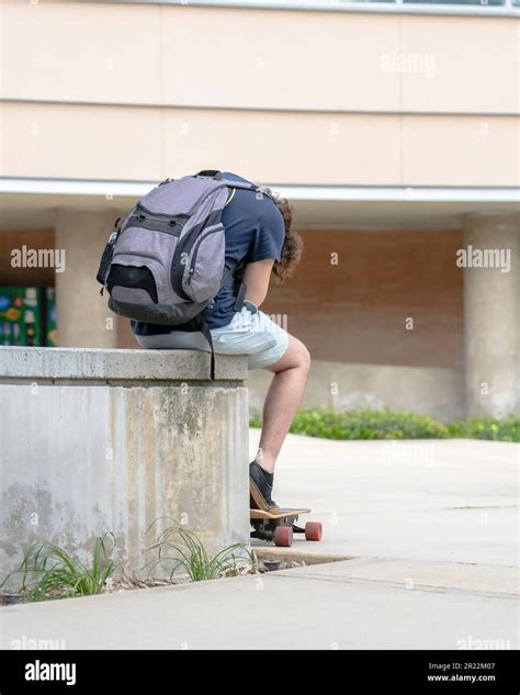 College Student Sitting Hunched Over With His Electric Skateboard And