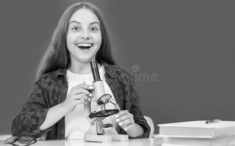 Happy Teen Girl Using Microscope In High School At Blackboard