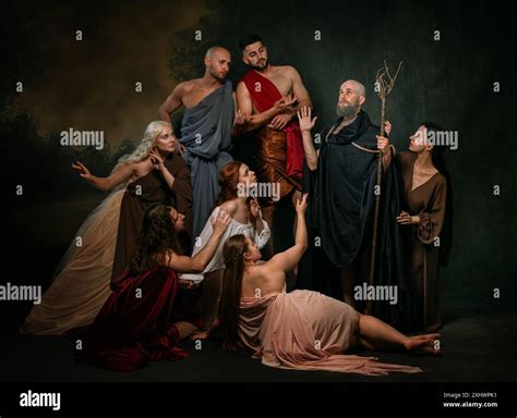 People In Classical Attire Gather Around Central Figure Holding Staff