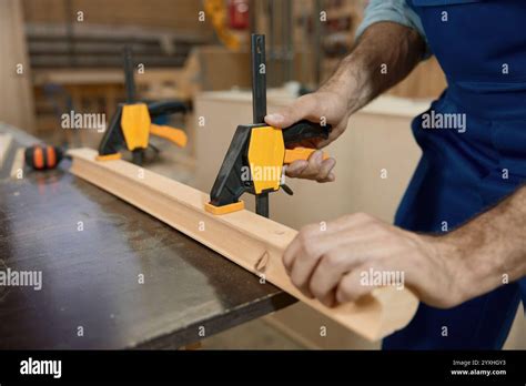 Carpenter Fixing Wooden Plank On Workbench With Clamps At Craft
