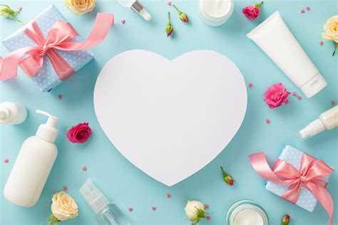텅 빈 흰색 하트가 있는 파스텔 블루 배경에 섬세한 장미 꽃 선물이 있는 정교한 크림 병 튜브 펌프 병 및 피펫이 평면적으로