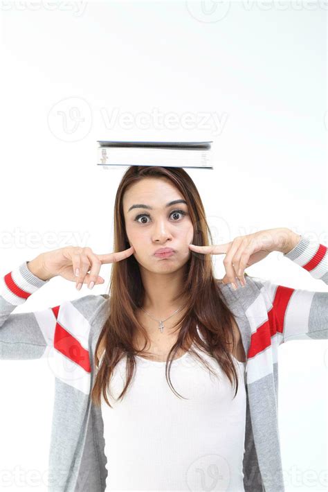 Yong Asian Youth Girl In Casual Dress Balancing Book On Head Look At Camera Finger On Cheek