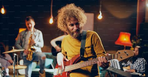 의자에 앉아 기타를 연주하는 베이스 기타리스트의 클로즈업 배경 색소폰 연주자와 피아노 연주자 홈 스튜디오 인테리어 사진 Unsplash의 음악가 이미지