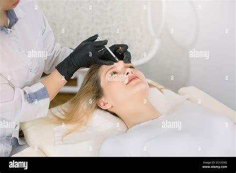 Hands Of Female Cosmetologist Making Botox Injection Between The Eyebrows On The Face Of A