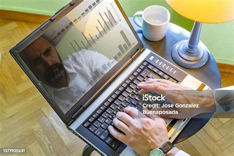 홈 인테리어의 전기 램프 옆에있는 작은 테이블에 위치한 노트북 키보드에서 비즈니스 임원의 남성 손 금융 차트에 남자의 얼굴을 반영 하는 노트북 화면 개념 집에서 일하기 실제