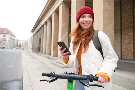 Premium Photo Redhead Girl Tourist With Backpack Uses Mobile Phone To Rent Escooter On Streets