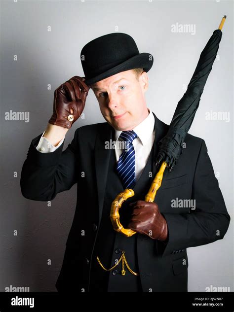Portrait Of British Businessman In Dark Suit Holding Umbrella And Politely Doffing Bowler Hat