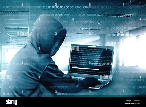 Hacker In Black Hoodie Using Laptop On The Desk To Hacking System With Binary Code And Upload
