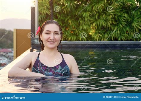 Woman In Swimsuit With Flower In Wet Hair Smiles And Looks At Camera