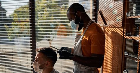 가위로 고객의 머리카락을 자르는 동안 보호용 안면 마스크와 멸균 장갑을 착용한 아프리카계 미국인 남성 이발사 사진 Unsplash의 이발사 이미지