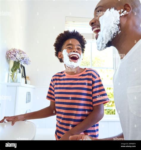 Father And Son At Home Having Fun Playing With Shaving Foam In Bathroom Making A Mess Together