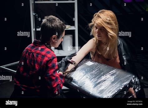 Eine Blonde Frau In Einem Tattoo Salon Macht Ein Tattoo Auf Ihrem Arm In Form Eines Wortes