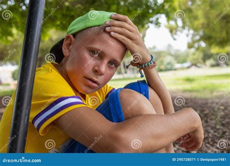 A Boy Of European Appearance In A Yellow T Shirt And A Green Cap Sits