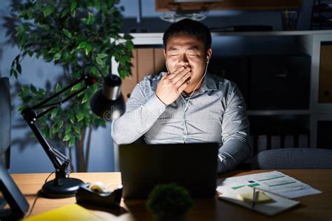Young Chinese Man Working Using Computer Laptop At Night Bored Yawning