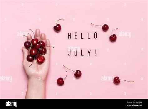 Hello July Text And Female Hand Holds Ripe Cherries On Pink Background Hello July Concept Stock