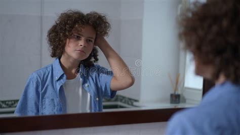 Reflection In Bathroom Mirror Of Concentrated Boy Touching Curly Hair
