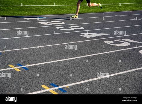 A Runner On A Gray Athletic Running Track With Large White Numbers Runner Races Over Numbers