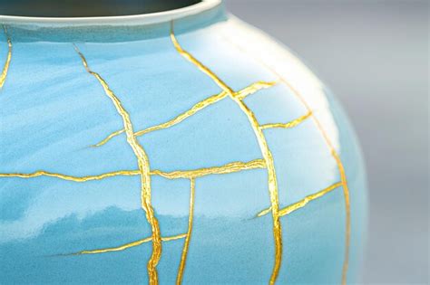 A Beautiful Kintsugi Vase Showcasing Golden Seams Against A Serene Blue