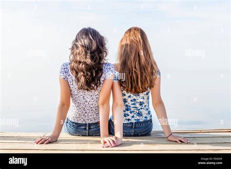 Two Girls Holding Hands Sitting Close Together At End Of A Dock
