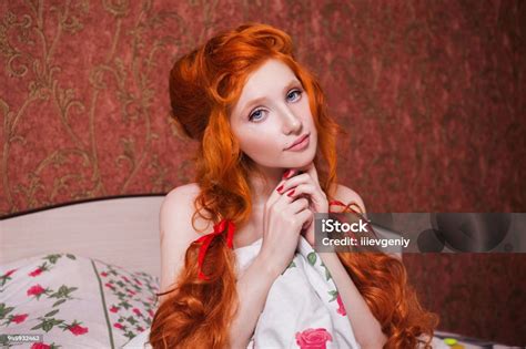 긴 붉은 곱슬 머리를 가진 여자는 담요 아래 침대에서 잠 옷에 머리 띠에 모였다 예쁜 얼굴 창백한 피부 파란 눈 및 침실에 밝은 특이 한 모양으로 빨간 머리 소녀 가정의