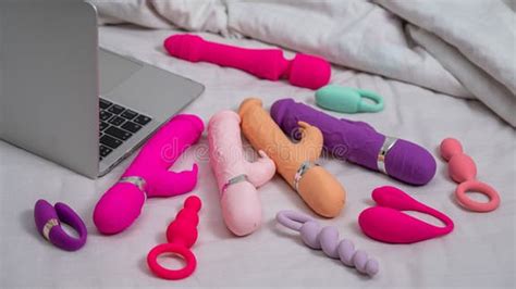 Collection Of Sex Toys On A White Sheet Various Vibrators And A Laptop
