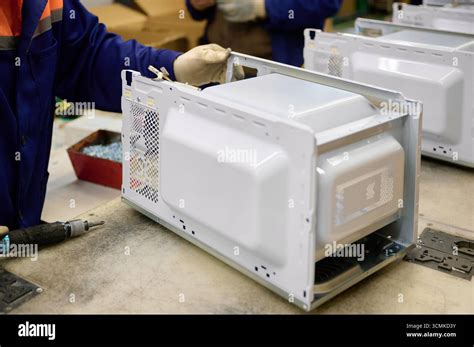Workers Assemble Microwave Ovens In A Factory Setting Focusing On Precision And Efficiency Stock